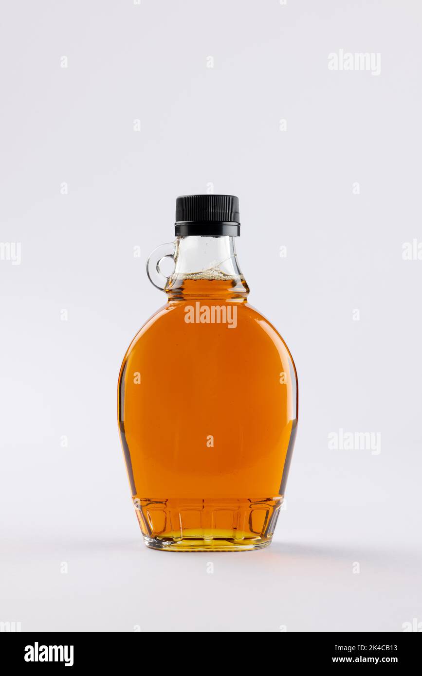 Vertical image of glass bottle of maple syrup on white background, with ...
