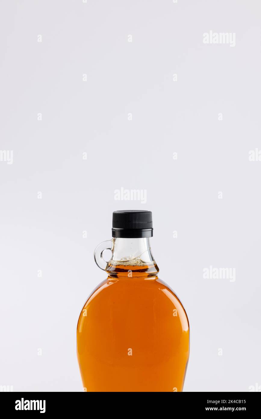 Vertical image of glass bottle of maple syrup on white background, with ...