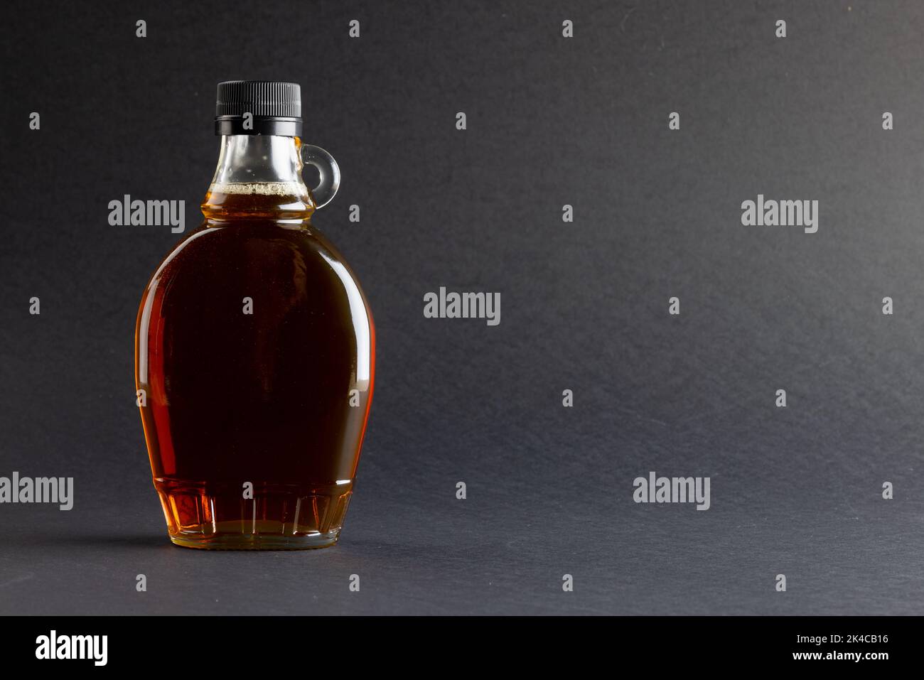 Horizontal image of glass bottle of maple syrup on dark grey background ...