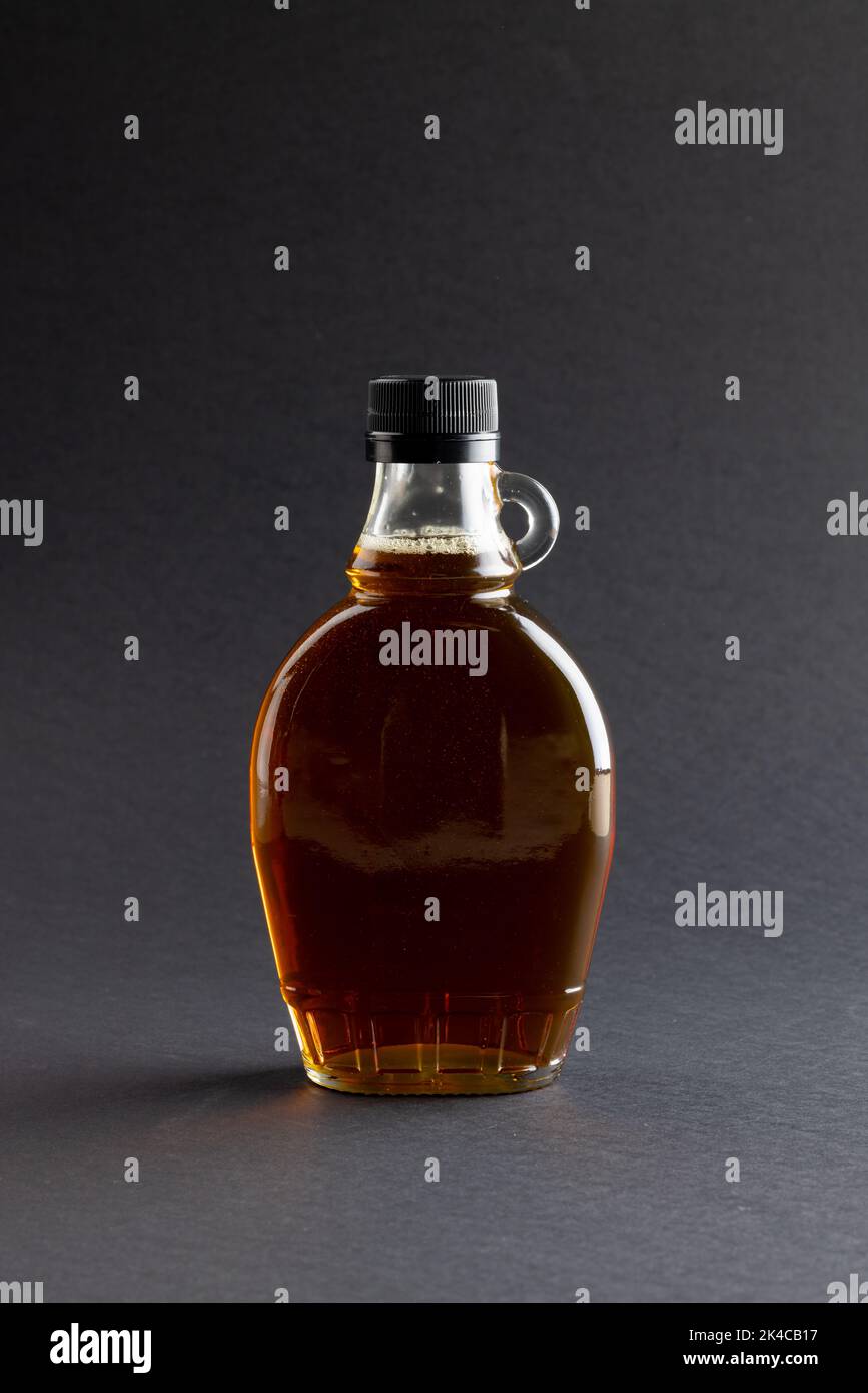Vertical image of glass bottle of maple syrup on dark grey background ...