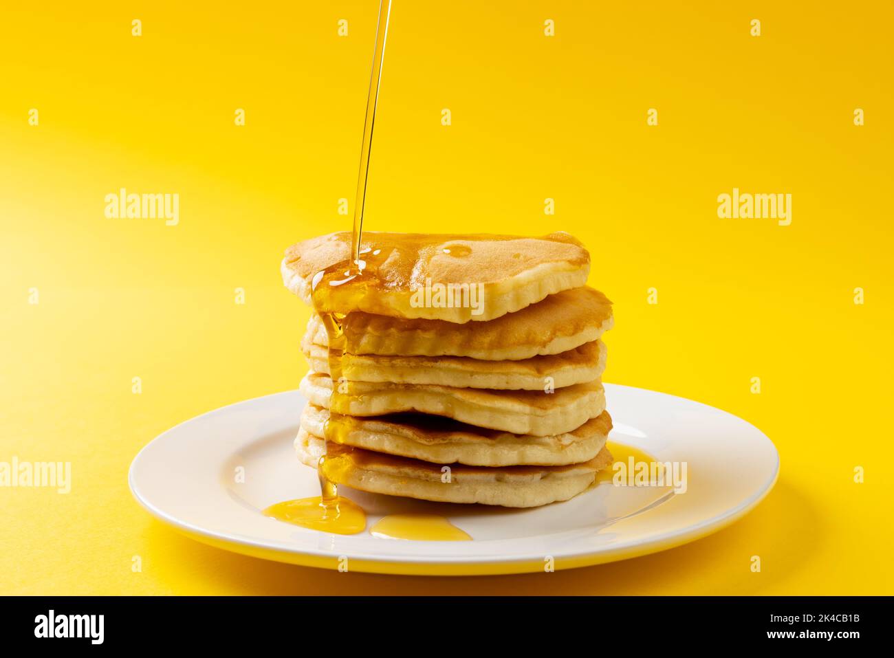 Horizontal image of maple syrup pouring onto stack of pancakes, yellow ...