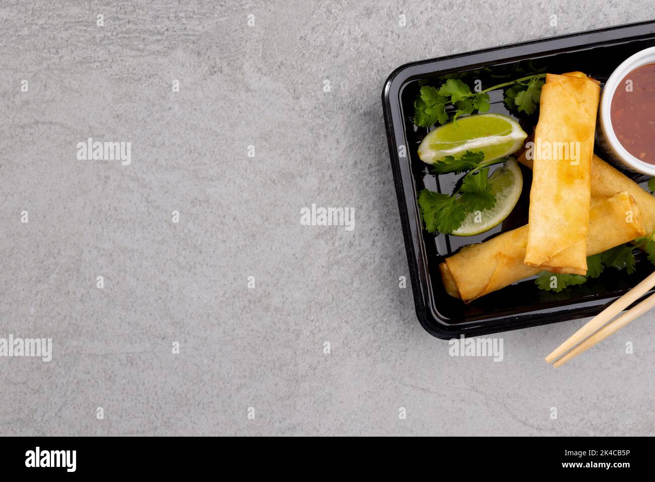 Overhead view of asian spring rolls, sliced lime, chilli sauce and ...