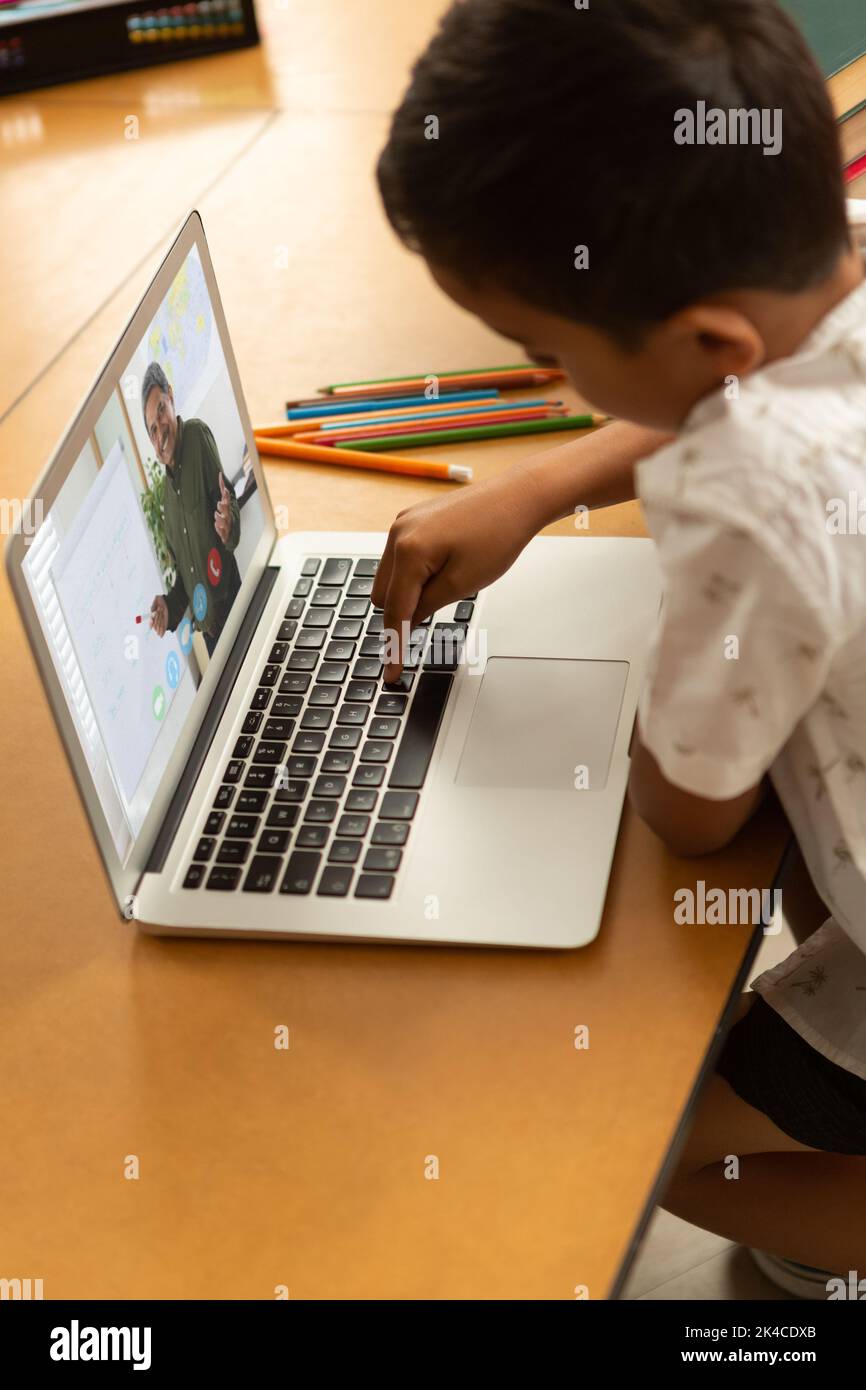Male student having a video call with male teacher on laptop at school ...