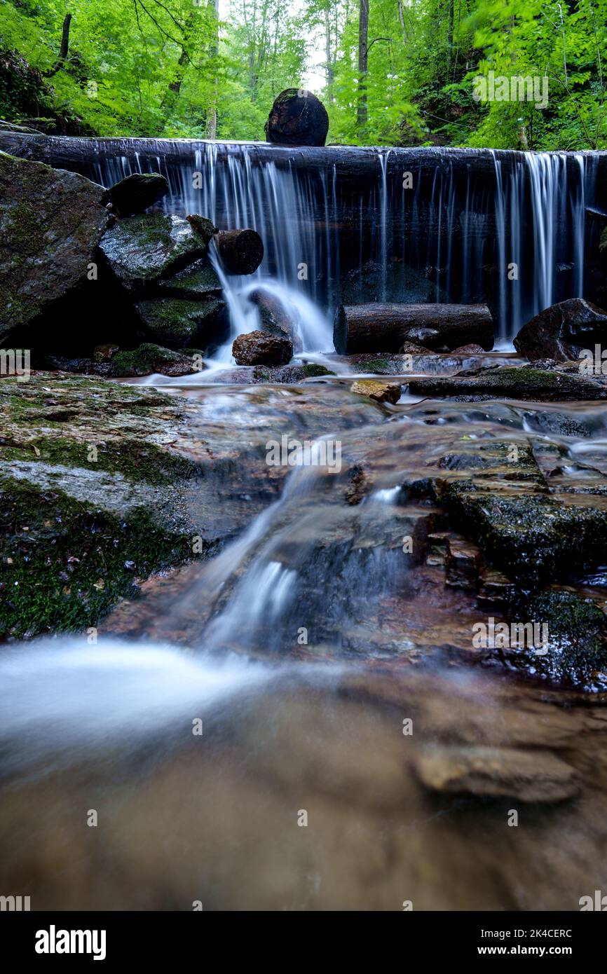 A long exposure shot of a small river cascade flowing down mossy rocks ...