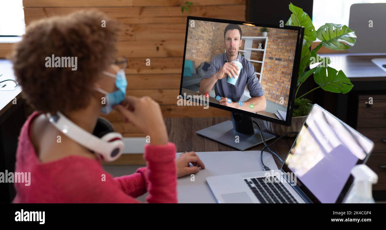African american businesswoman wearing face mask sitting at desk using ...