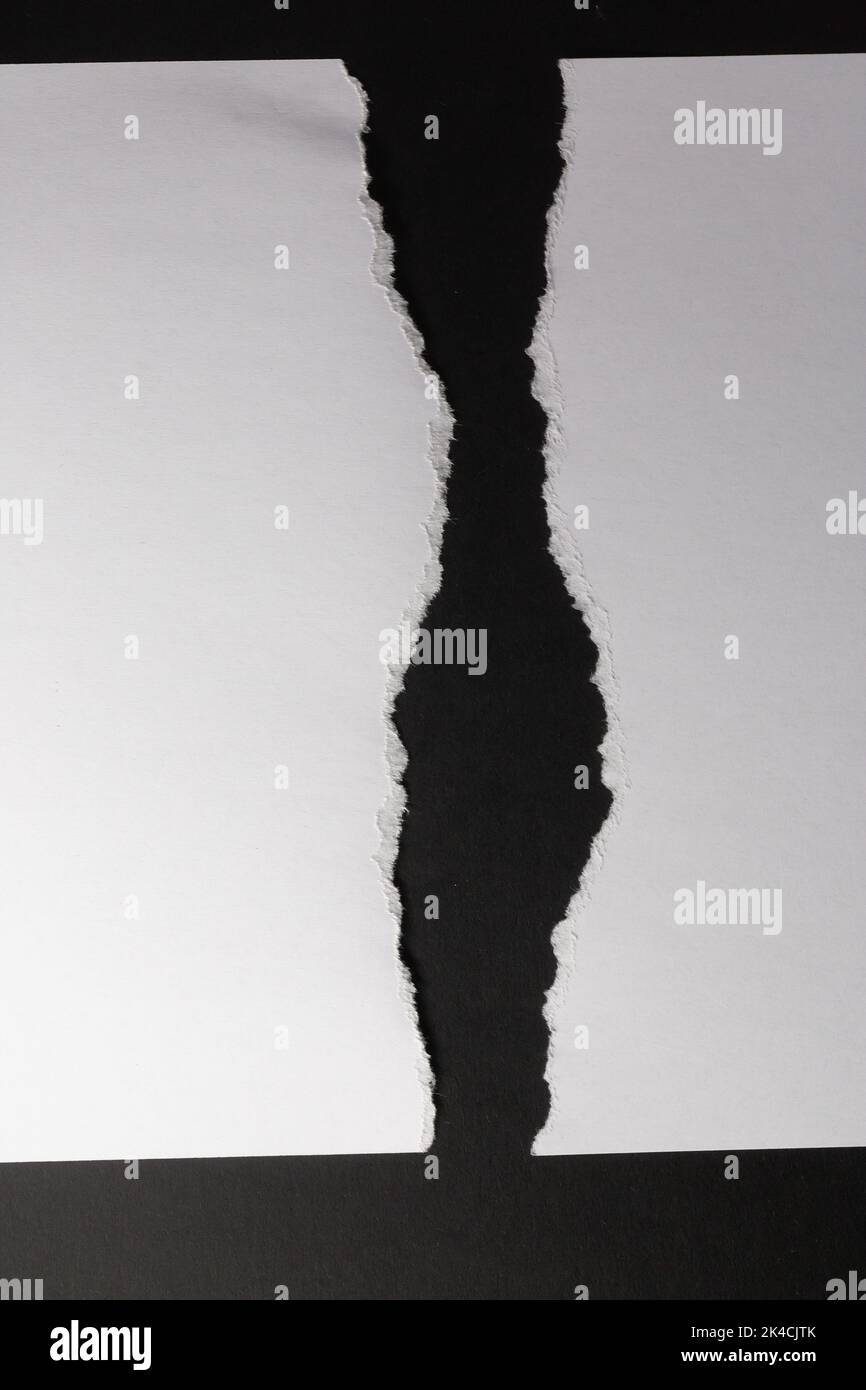 Two sheets of white paper with torn edges facing, on black background ...