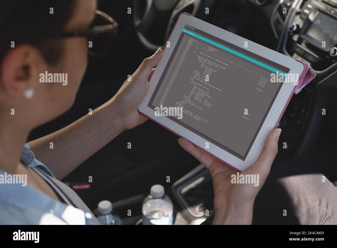 Biracial female programmer sitting in car, holding tablet with coding on screen. coding ...