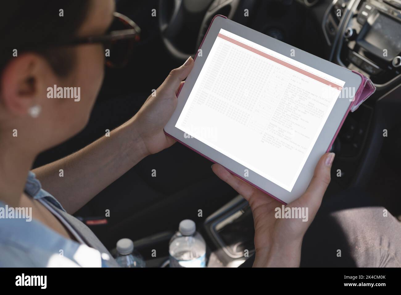 Biracial female programmer sitting in car, holding tablet with copy space on screen. coding ...