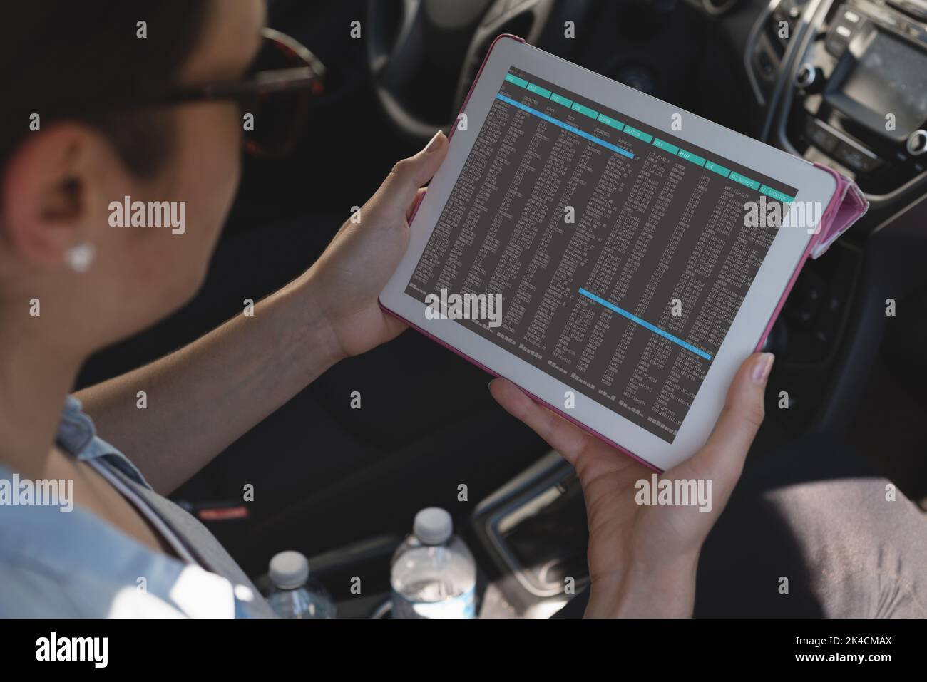Biracial female programmer sitting in car, using tablet with coding on screen. coding ...