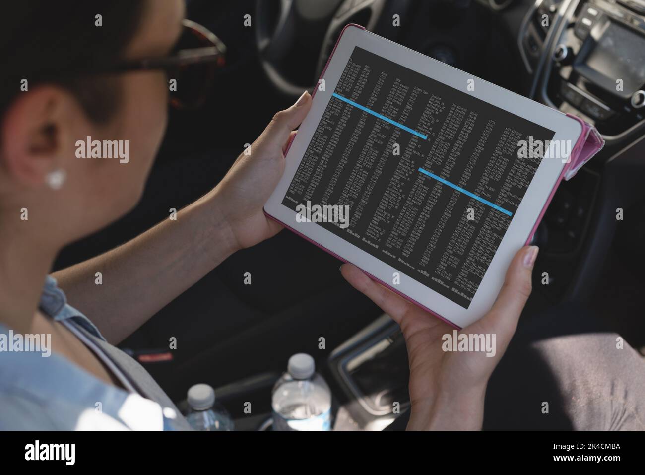 Biracial female programmer sitting in car, using tablet with coding on ...