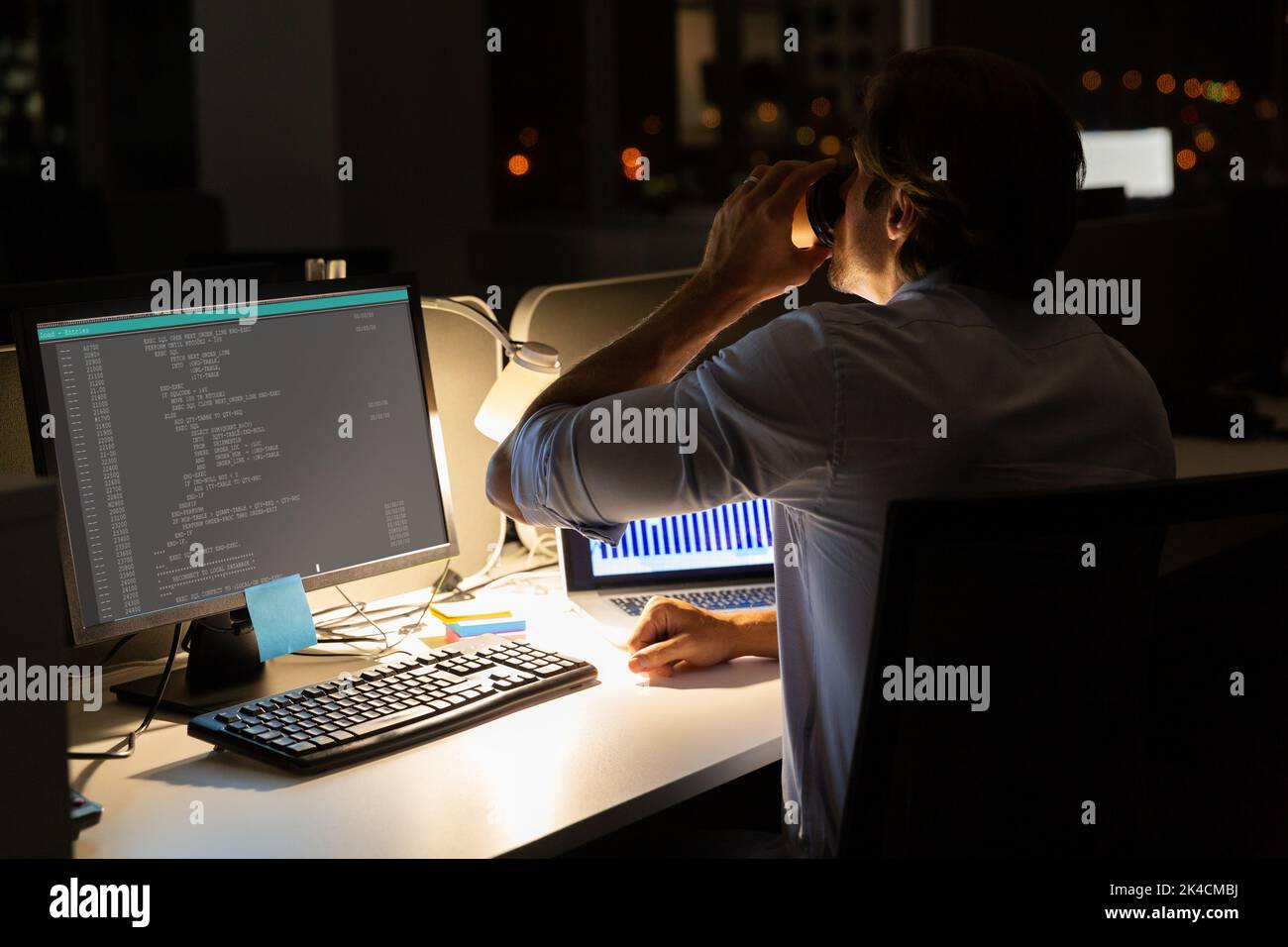 Caucasian male programmer sitting at desk, drinking coffee, using ...