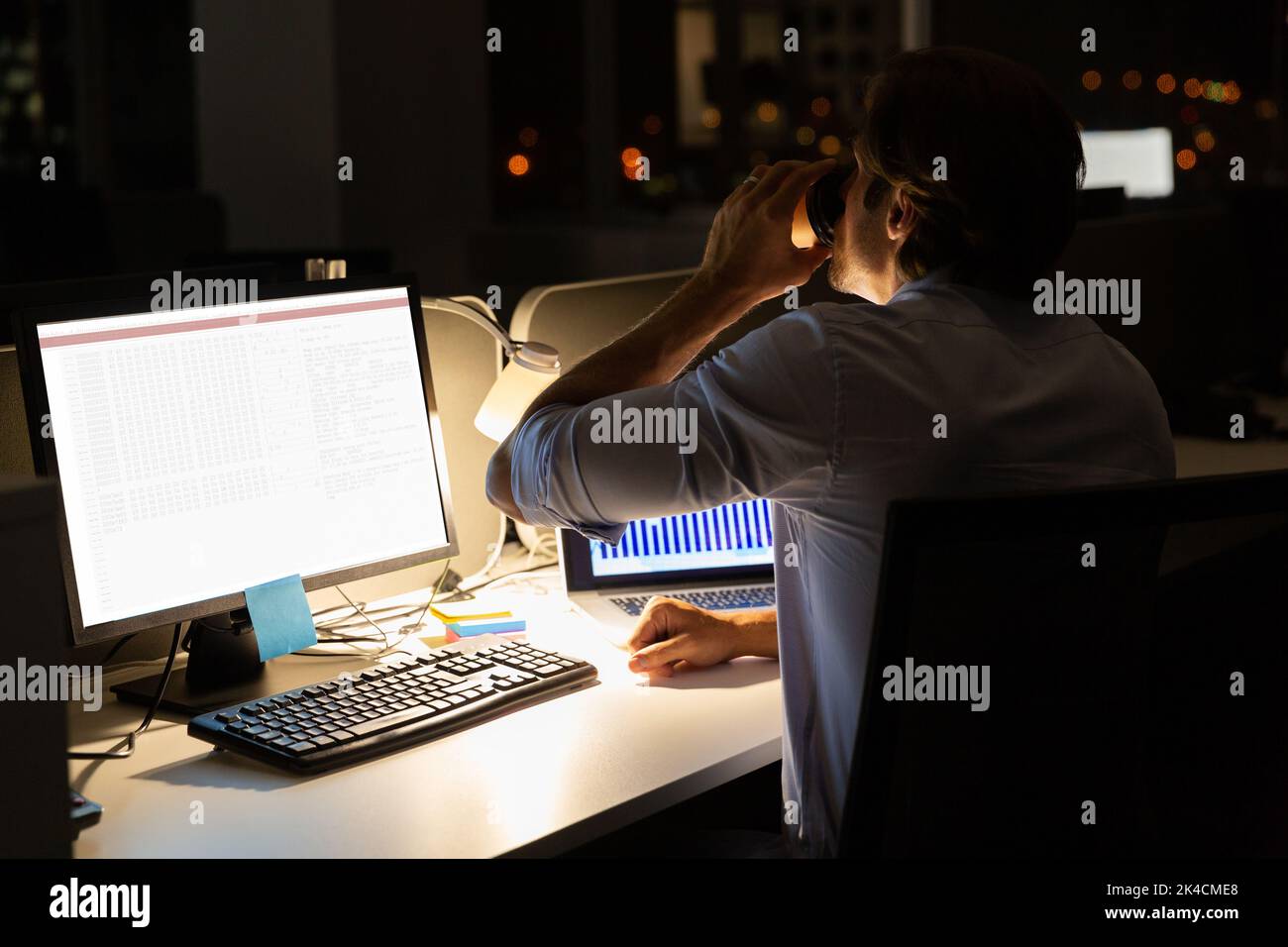 Caucasian Male Programmer Sitting At Desk Drinking Coffee Using Computer With Coding On Screen