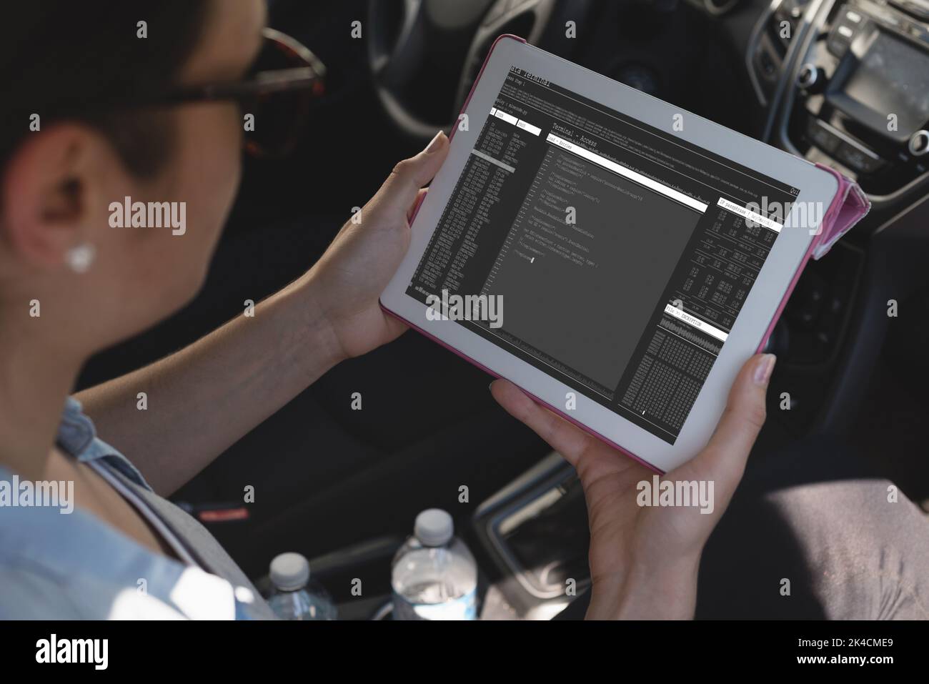 Biracial female programmer sitting in car, using tablet with coding on screen. coding ...