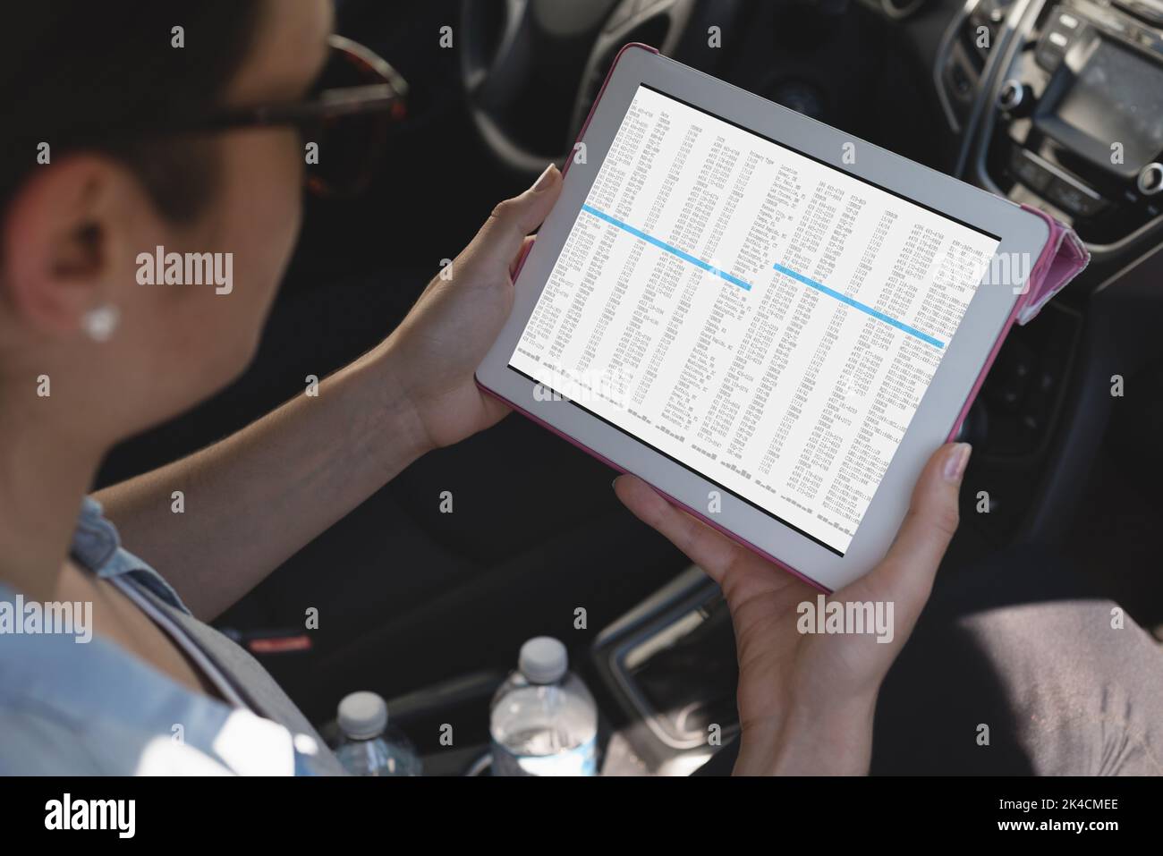 Biracial female programmer sitting in car, using tablet with coding on ...