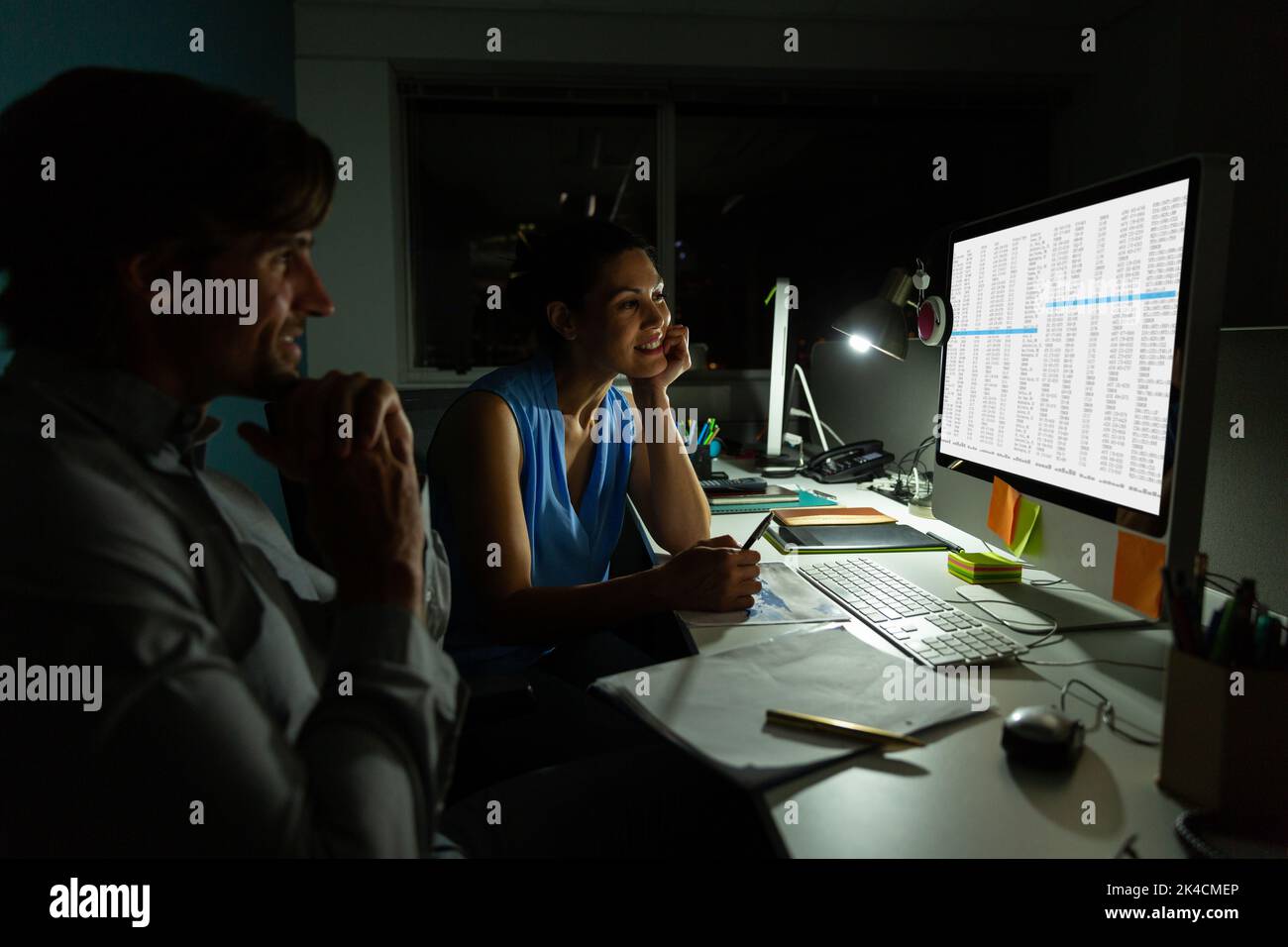 Two diverse male and female colleagues sitting at desk, using computer with coding on screen ...