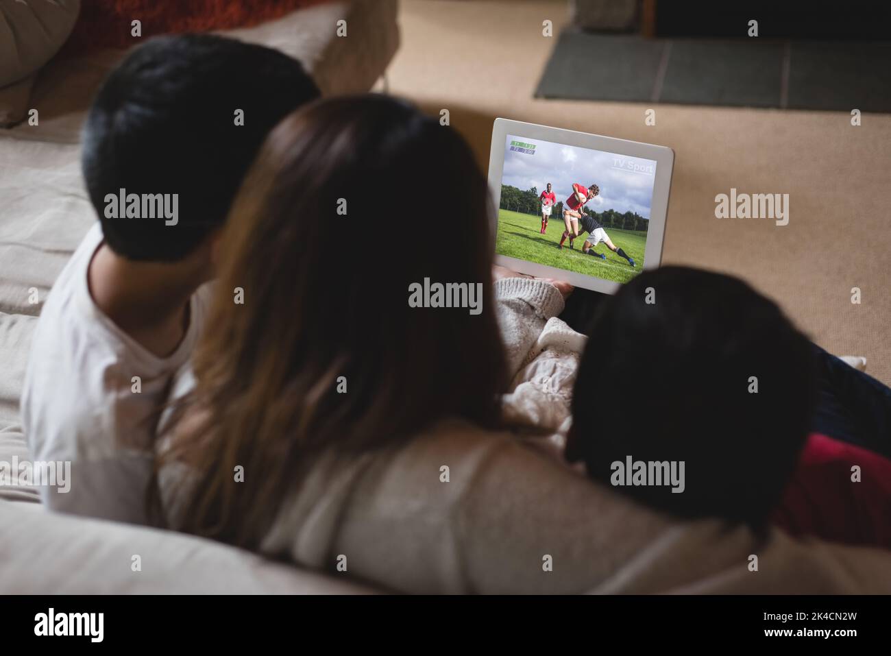 Back view of latin mother and children watching rugby match on laptop ...