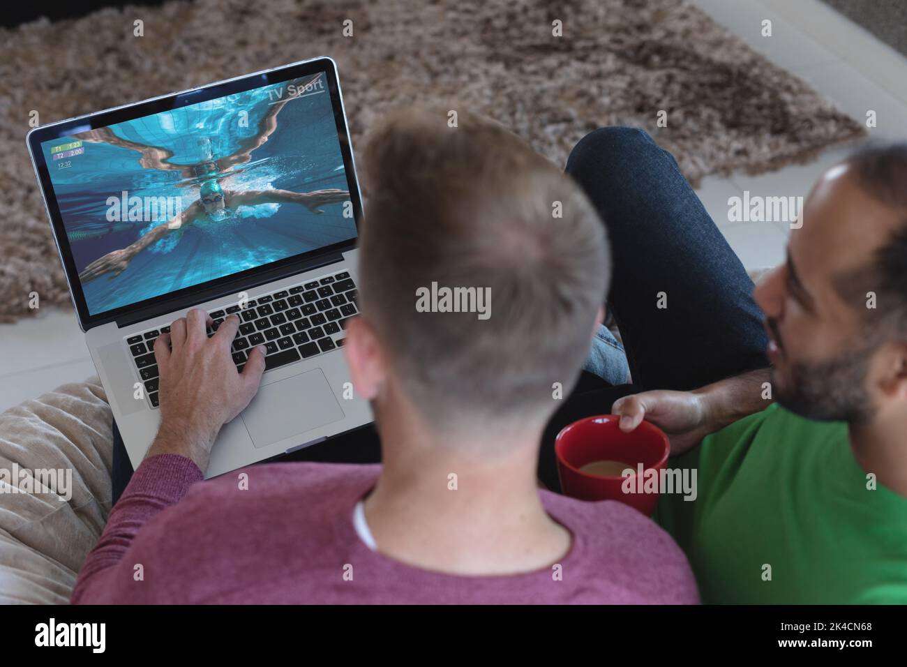 Two diverse male friends at home watching swimming competition on ...