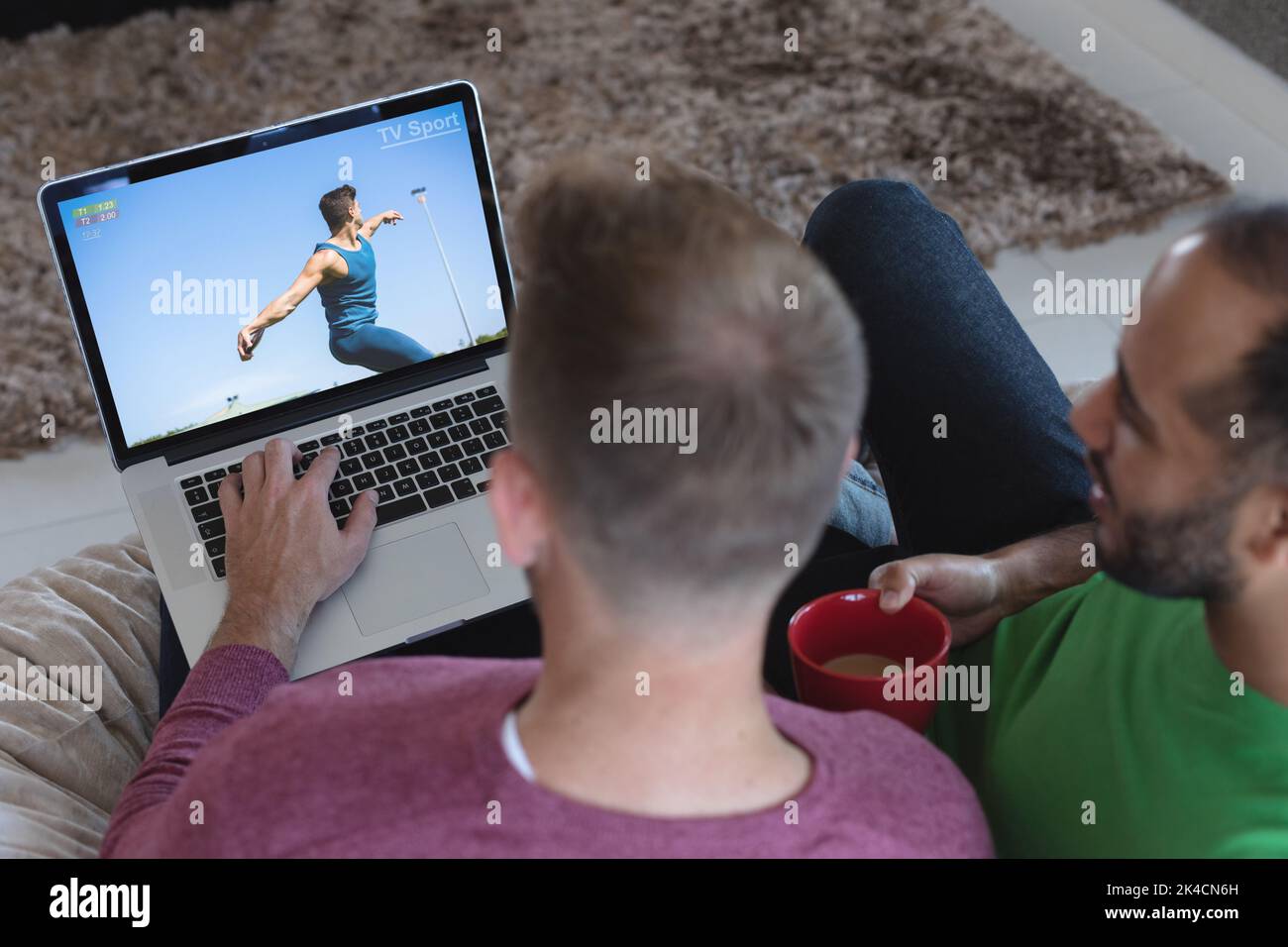 Two diverse male friends at home watching male athlete throwing discus ...