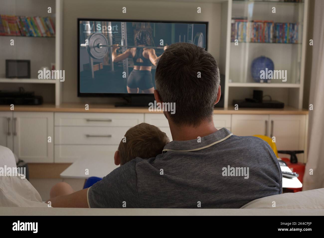 Rear view of father and son sitting at home together watching sport ...
