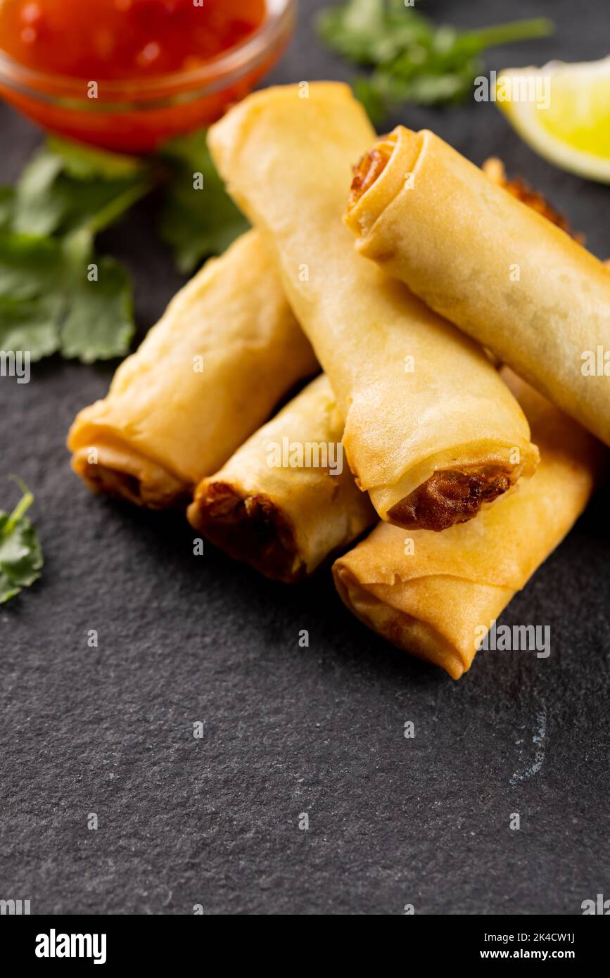 Close up of asian spring rolls, sliced lime and chilli sauce on grey ...