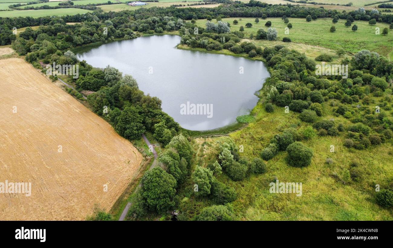 An aerial view of a lake between green fields with trees and bushes in ...