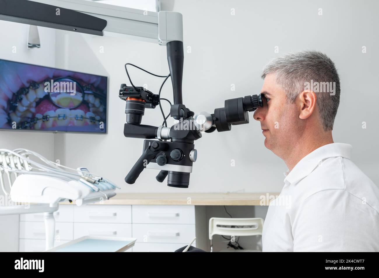 Dentist using dental microscope treating patient teeth at dental clinic ...