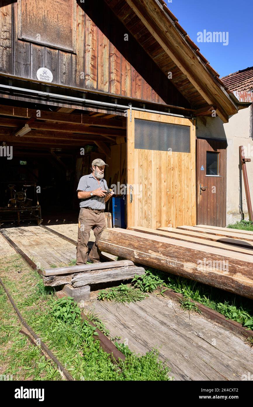 A carpenter working standing outside of the sawmill on a sunny day with ...
