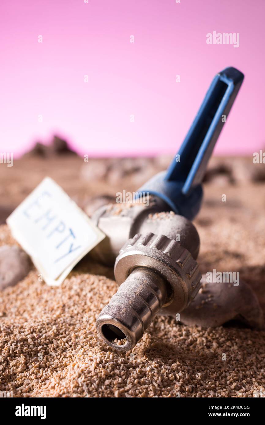 Vertical close-up of a dry open faucet buried by desert sand with a ...