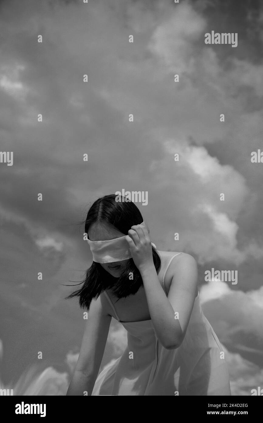 A vertical greyscale shot of a female with eyes closed with a cloth ...