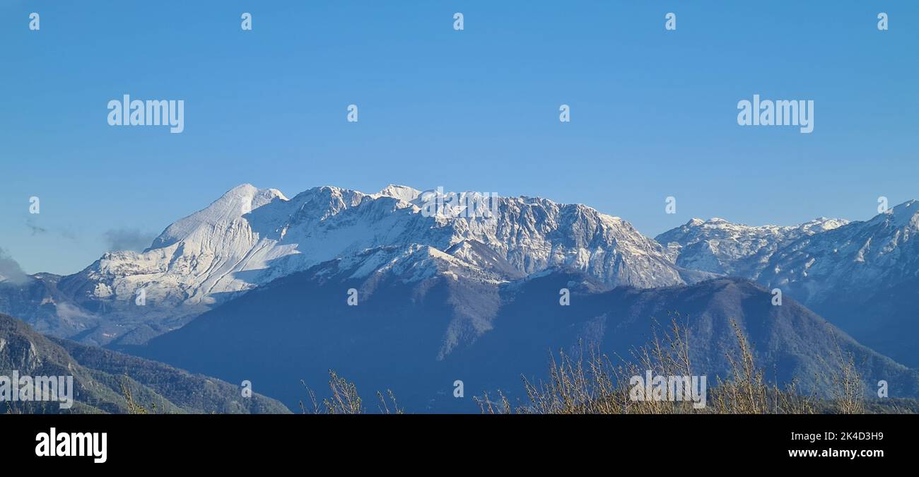 A scenic view of snowy mountains under sunlight with forests around ...