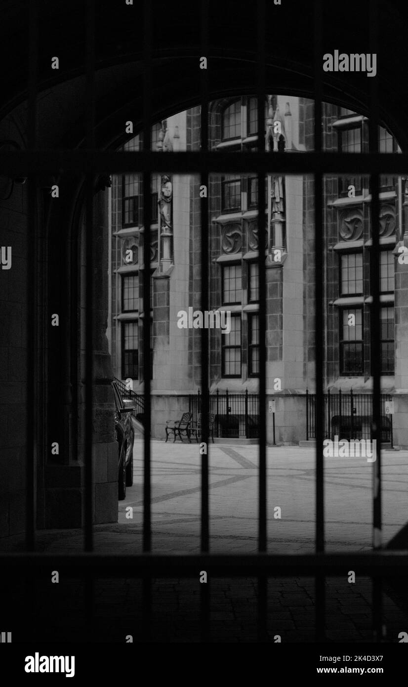 A grayscale of a building behind the arch bars with a parked car and a ...