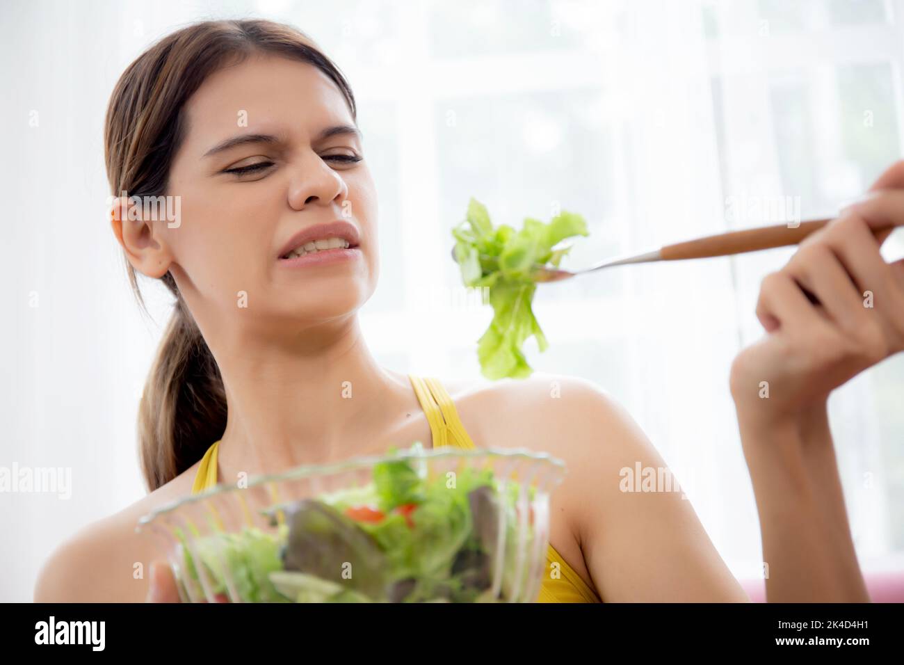 Young caucasian woman sitting on sofa eating vegetable salad while ...