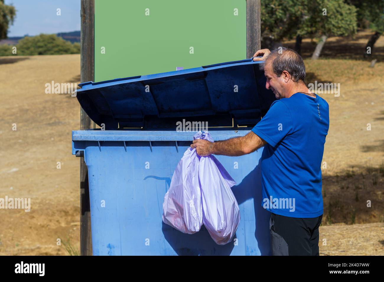 man throwing garbage bags into a dumpster with a blank sign for copy ...