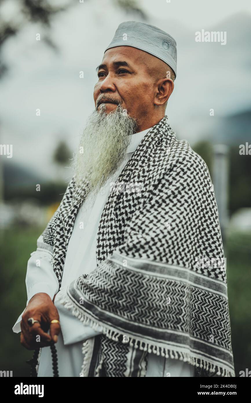 A vertical side closeup of a Muslim male with a white beard wearing a ...
