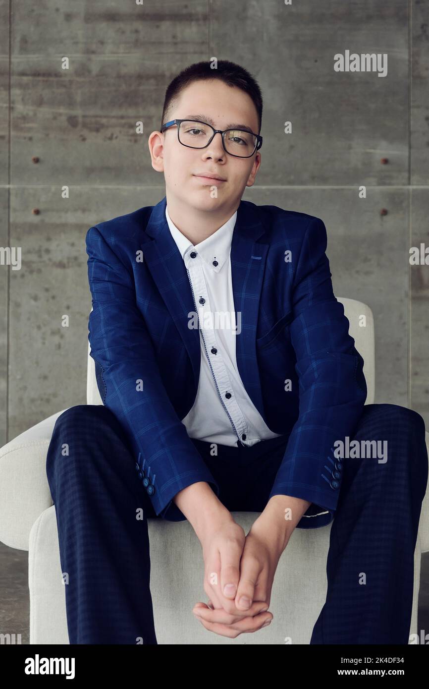 a boy with glasses with an intelligent look sits in a chair with his ...
