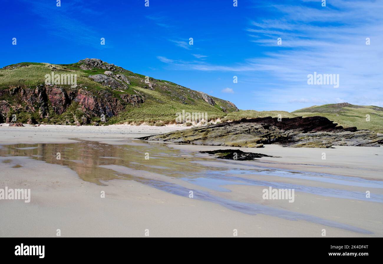Small cliff and blue sky reflected in water on white sand beach at ...