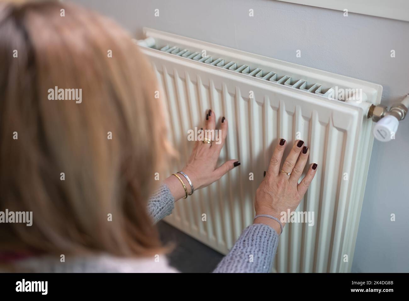 Woman with her hands glued to a radiator to warm them by the cold of ...