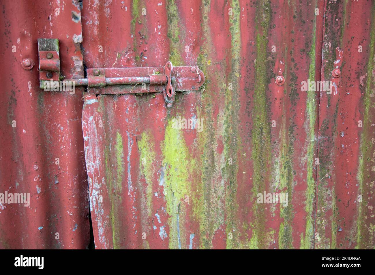 Close up shot of a red-painted corrugated-metal barn door with copious ...