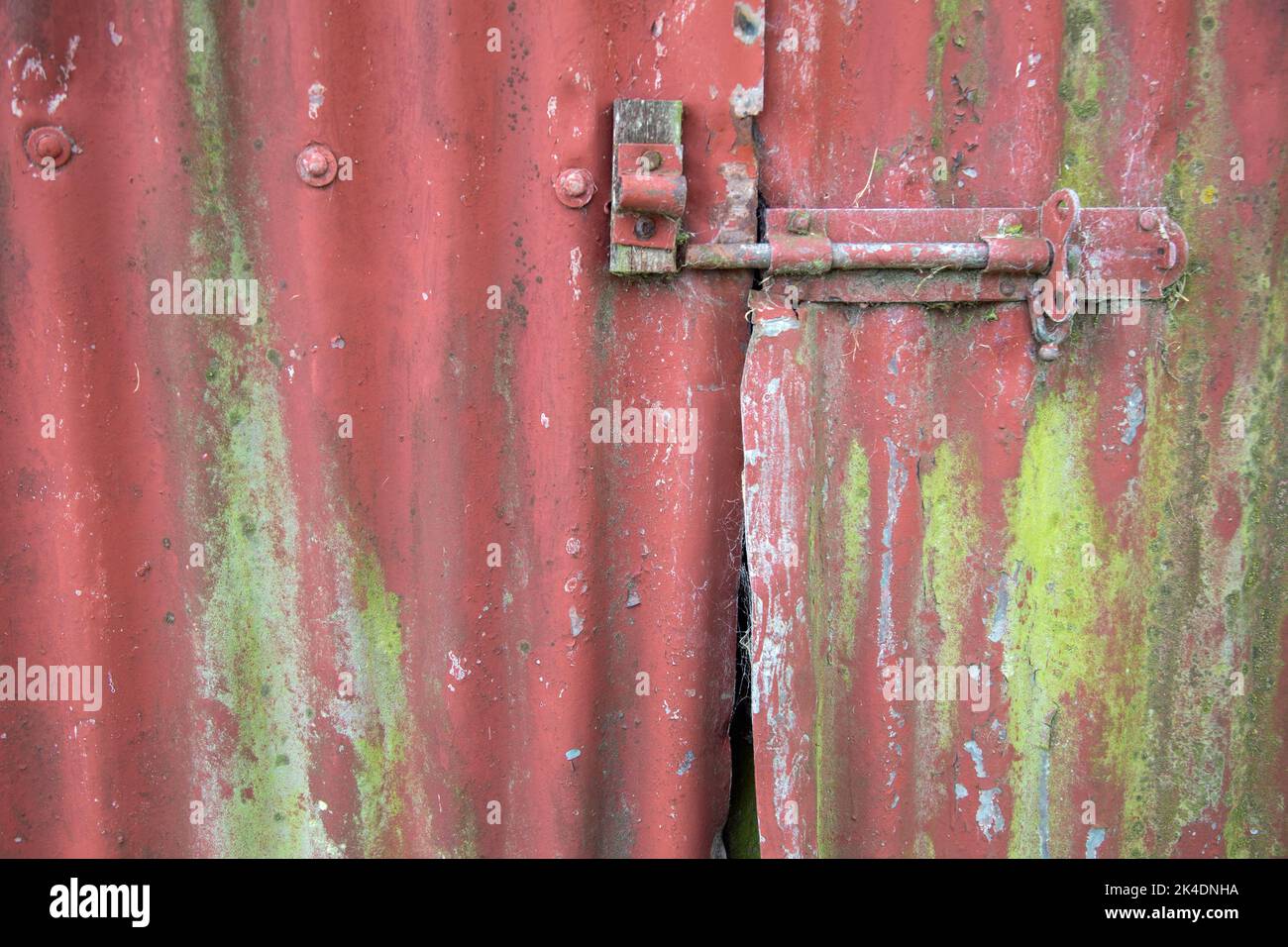 Close up shot of a red-painted corrugated-metal barn door with copious ...