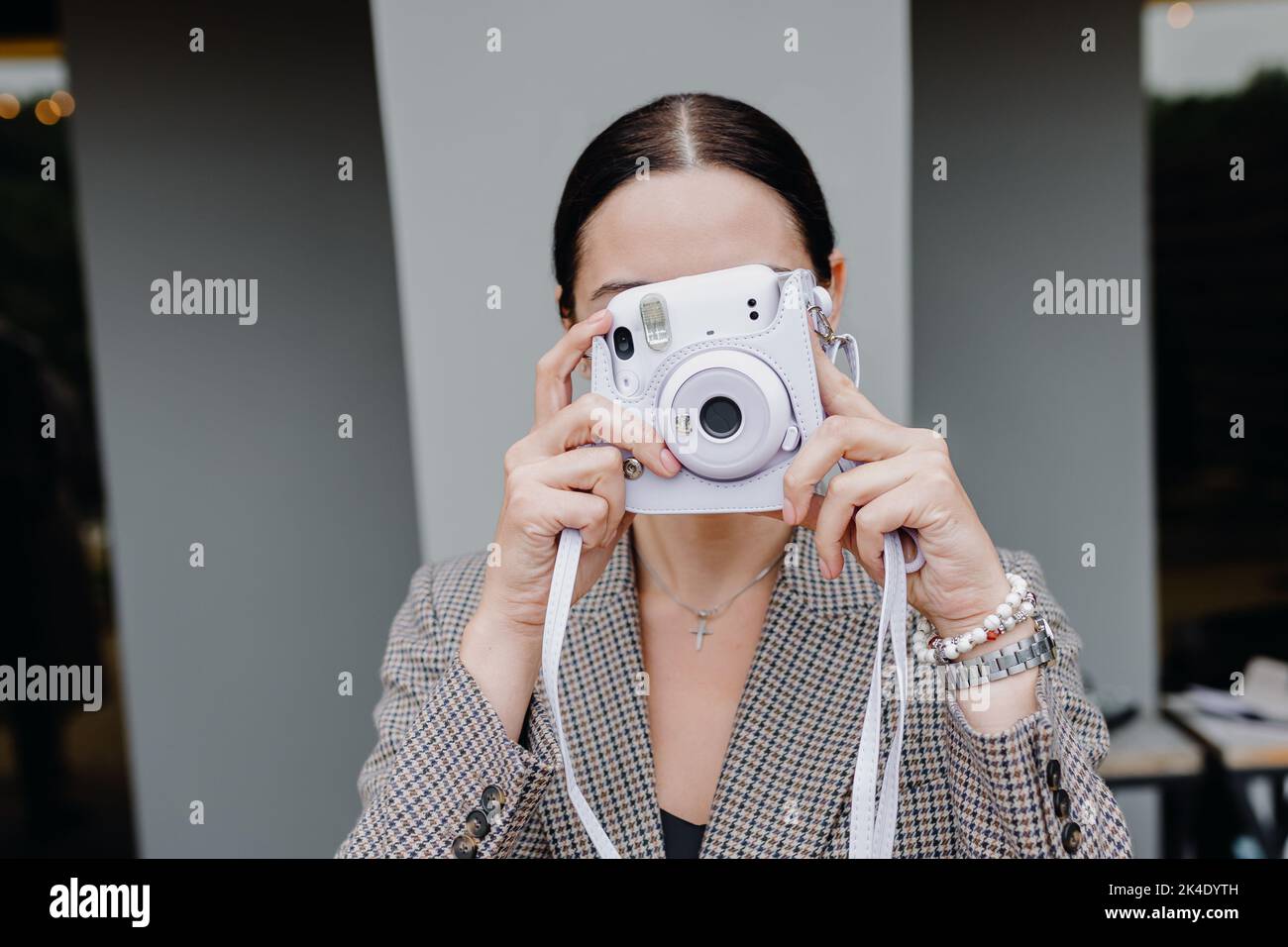A young brunette girl poses with a polaroid camera against a gray wall ...