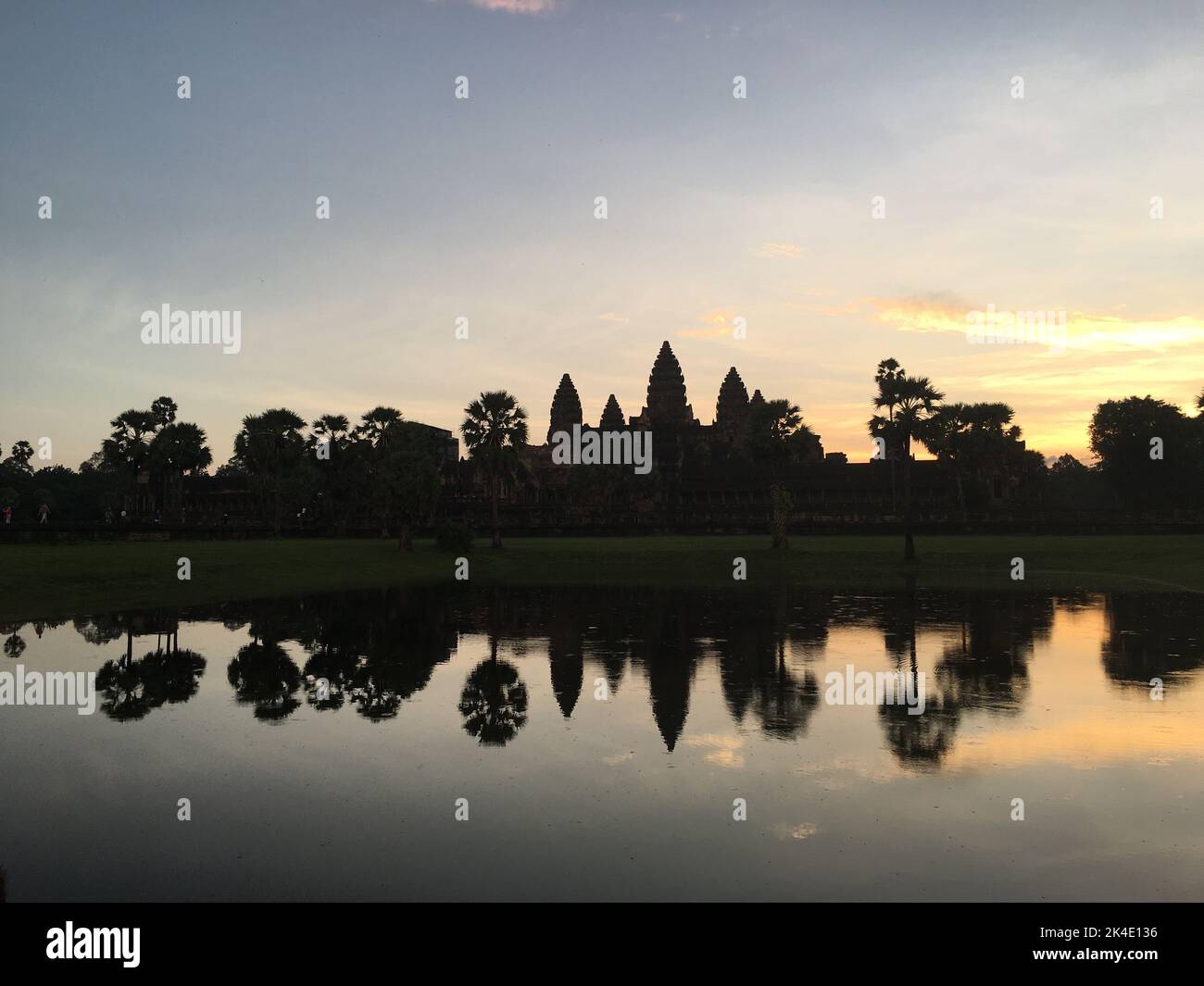 A lake reflecting Angkor Wat temple silhouettes at sunset with purple ...