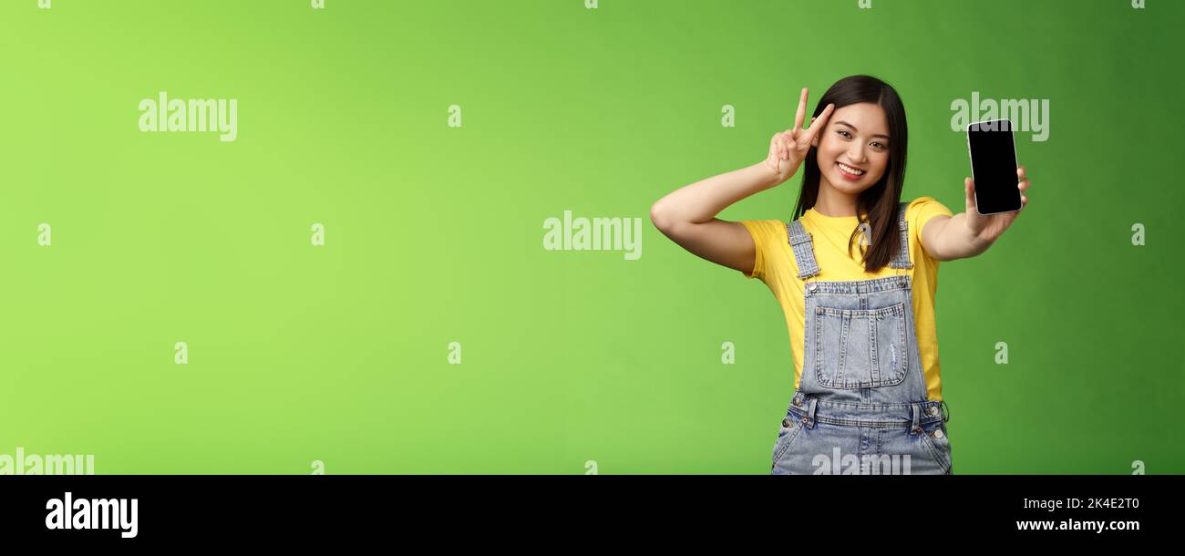 Cute carefree asian brunette showing application on smartphone screen ...