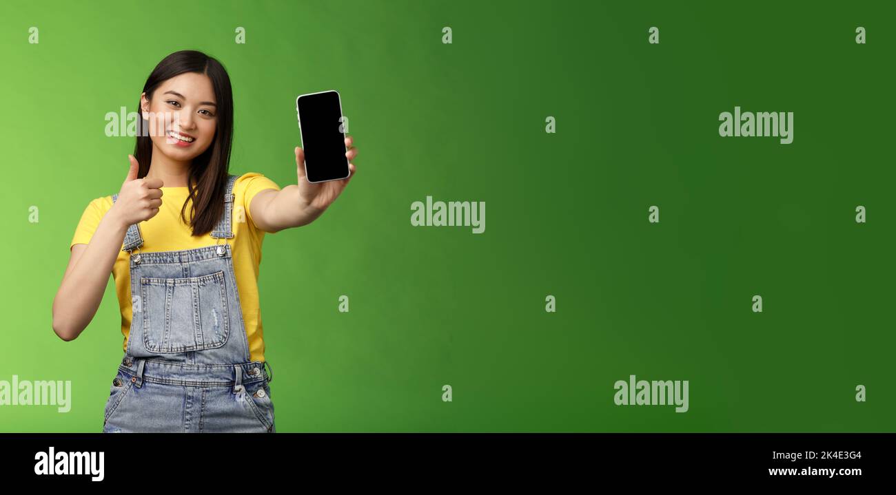 Cheerful cute asian woman judging good smartphone game, show thumb-up ...