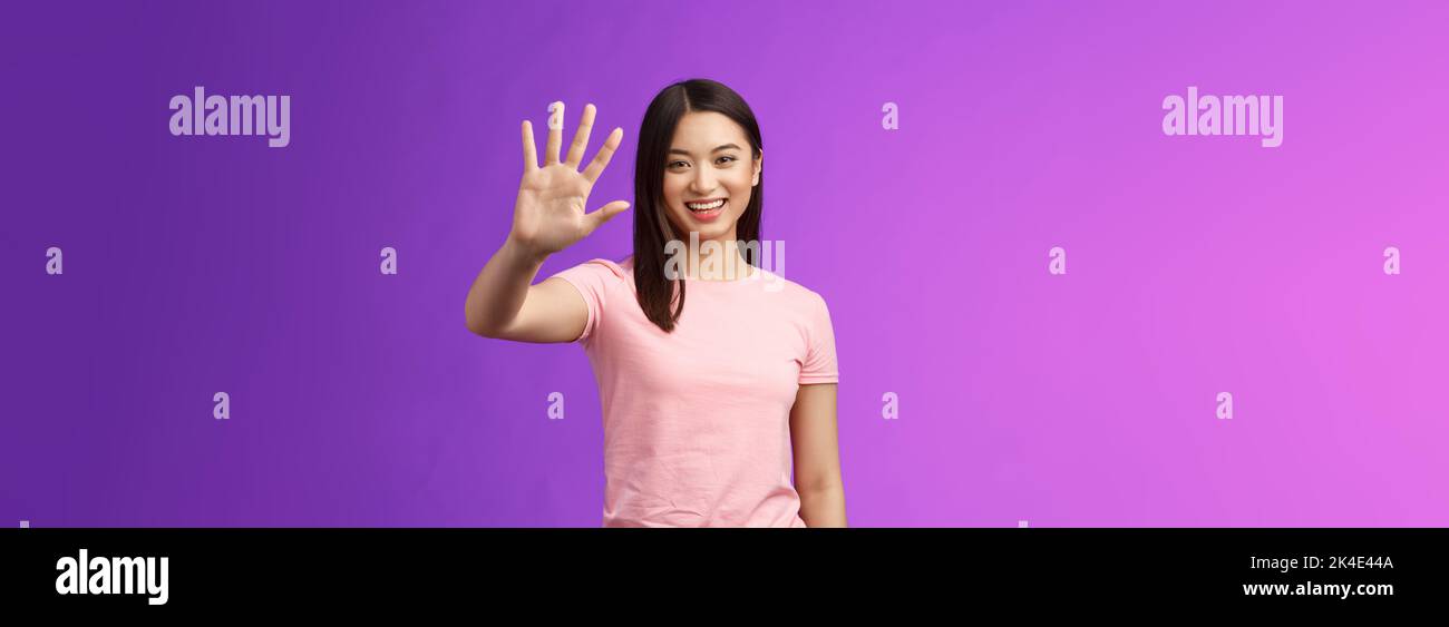 Friendly cute asian tender girl raise palm waving goodbye, smiling ...