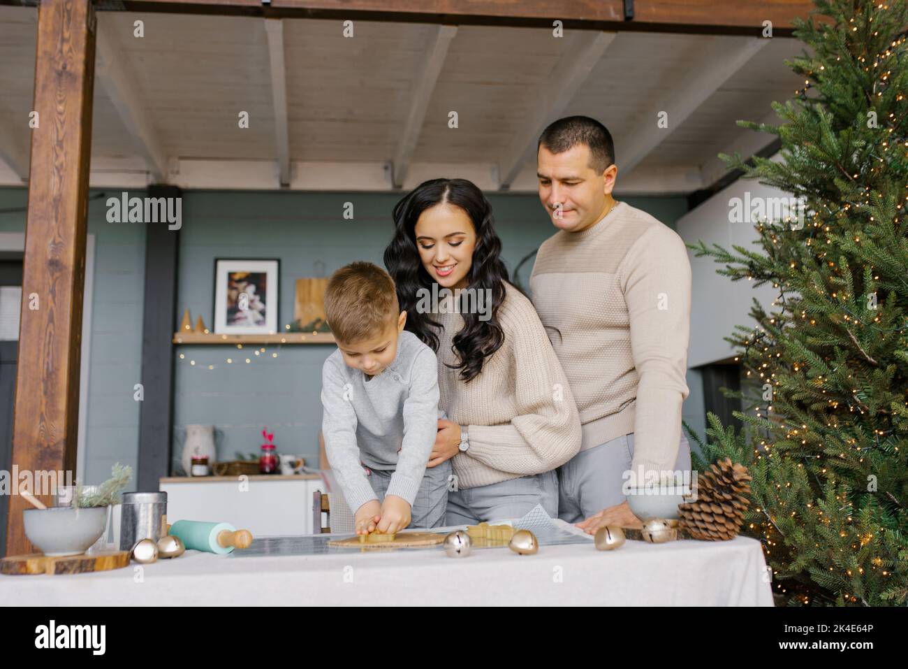 Mom, dad and little son cut out shapes from dough for ginger cookies or ...
