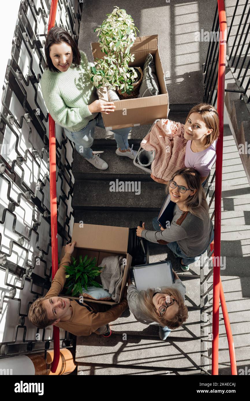 Vertical smiling anticipating student friends carrying boxes with ...
