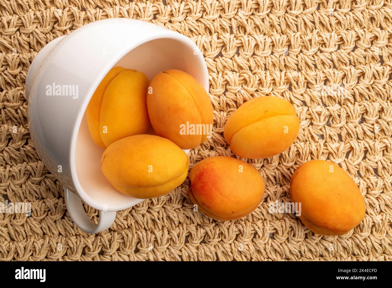 Several yellow pineapple apricots in a white cup, close-up, on a straw ...