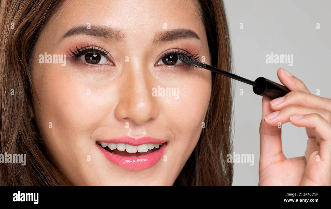 Closeup ardent young woman putting mascara on her long eyelashes with ...