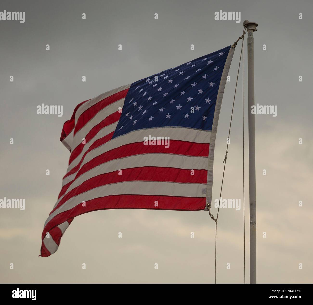 American flag proudly waving with clouds behind at sunset Stock Photo ...
