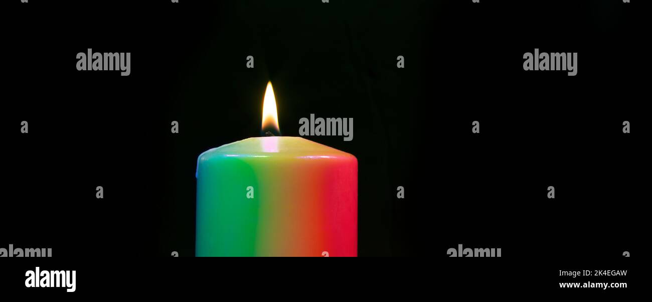 Rainbow colored candle burning on a black background Stock Photo - Alamy